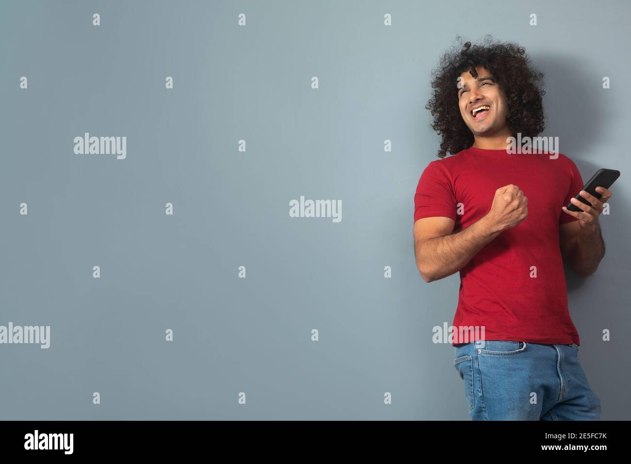 A CURLY HAIRED MAN SCREAMING IN JOY WHILE USING MOBILE PHONE Stock ...