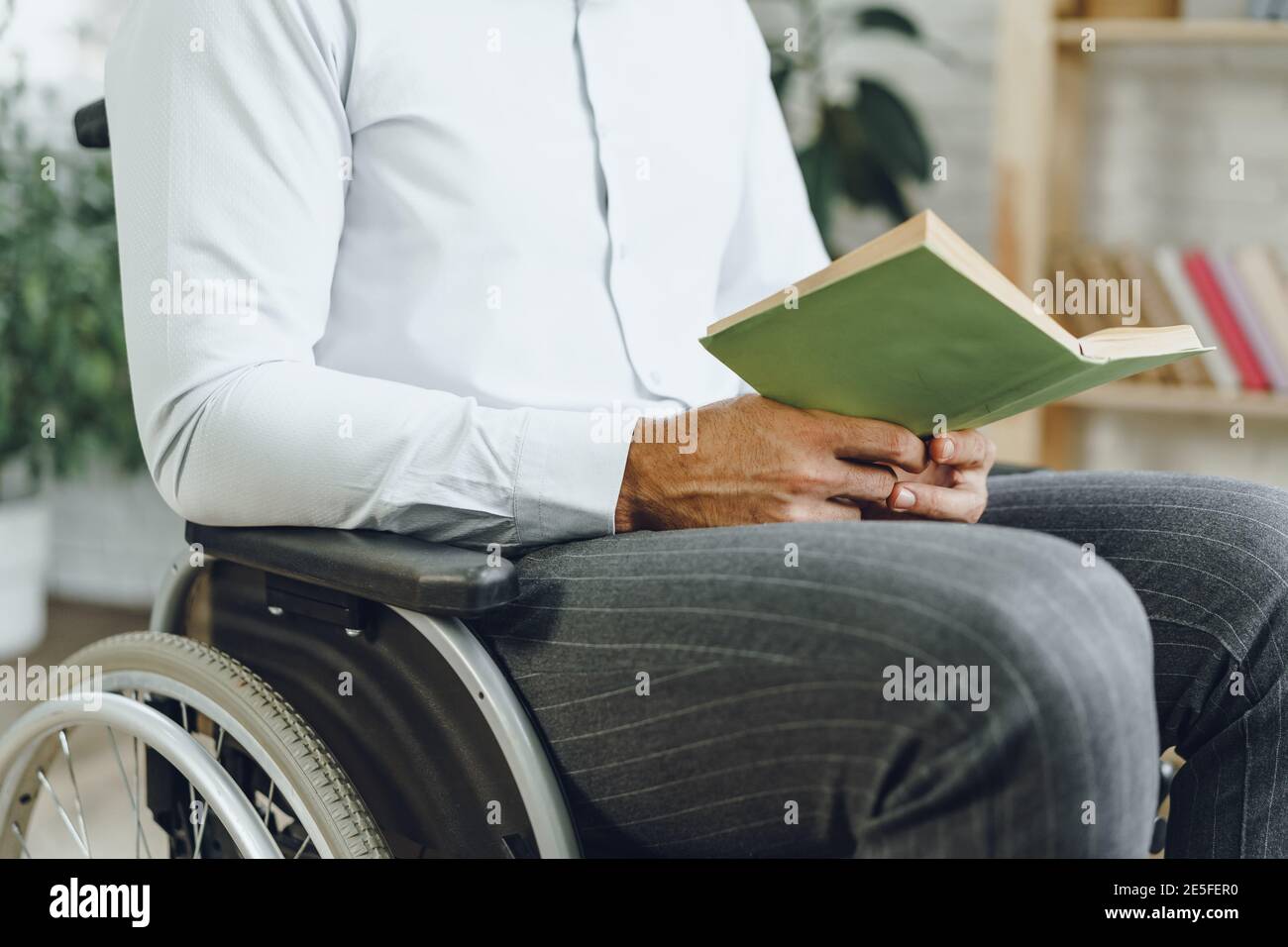 Disabled man in wheelchair reading a book indoors Stock Photo - Alamy