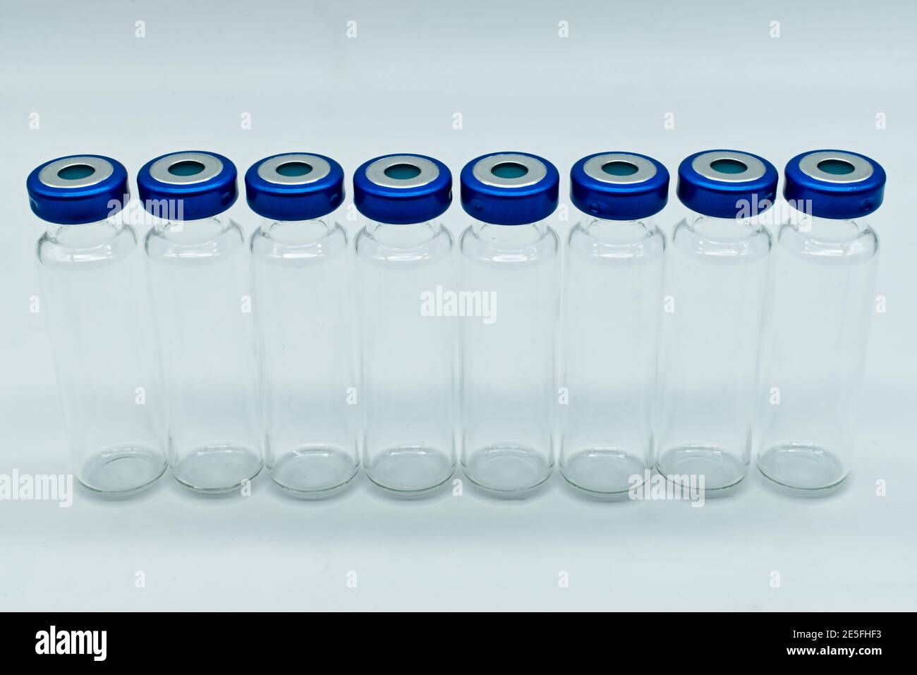 Row of transparent glass medical vials for injection with blue sealed ...