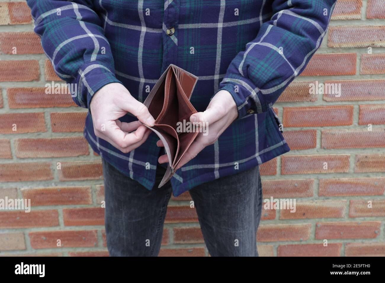Man with no money showing empty wallet with brick wall behind Stock ...