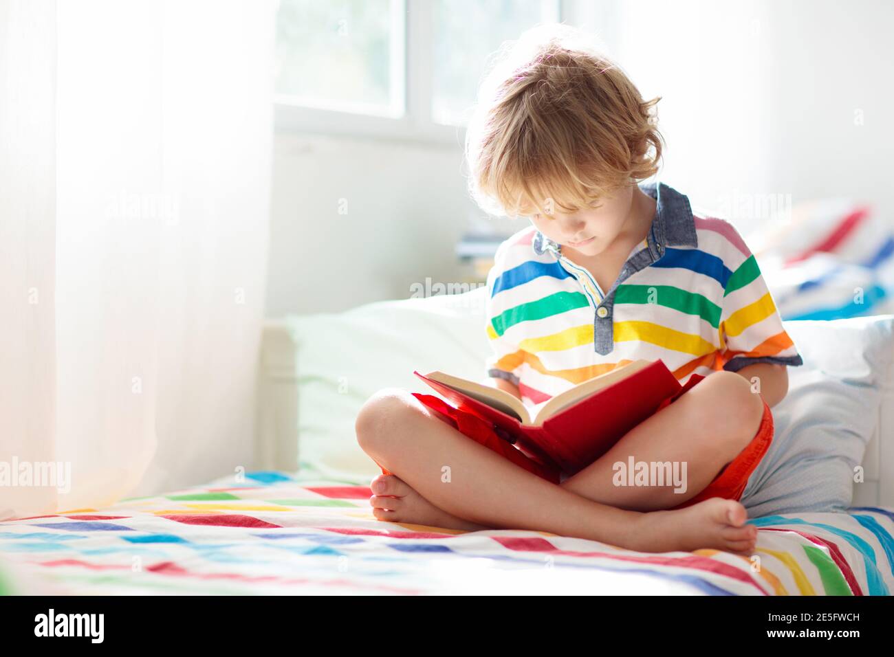 Child reading book in bed in white sunny bedroom with window. Children ...