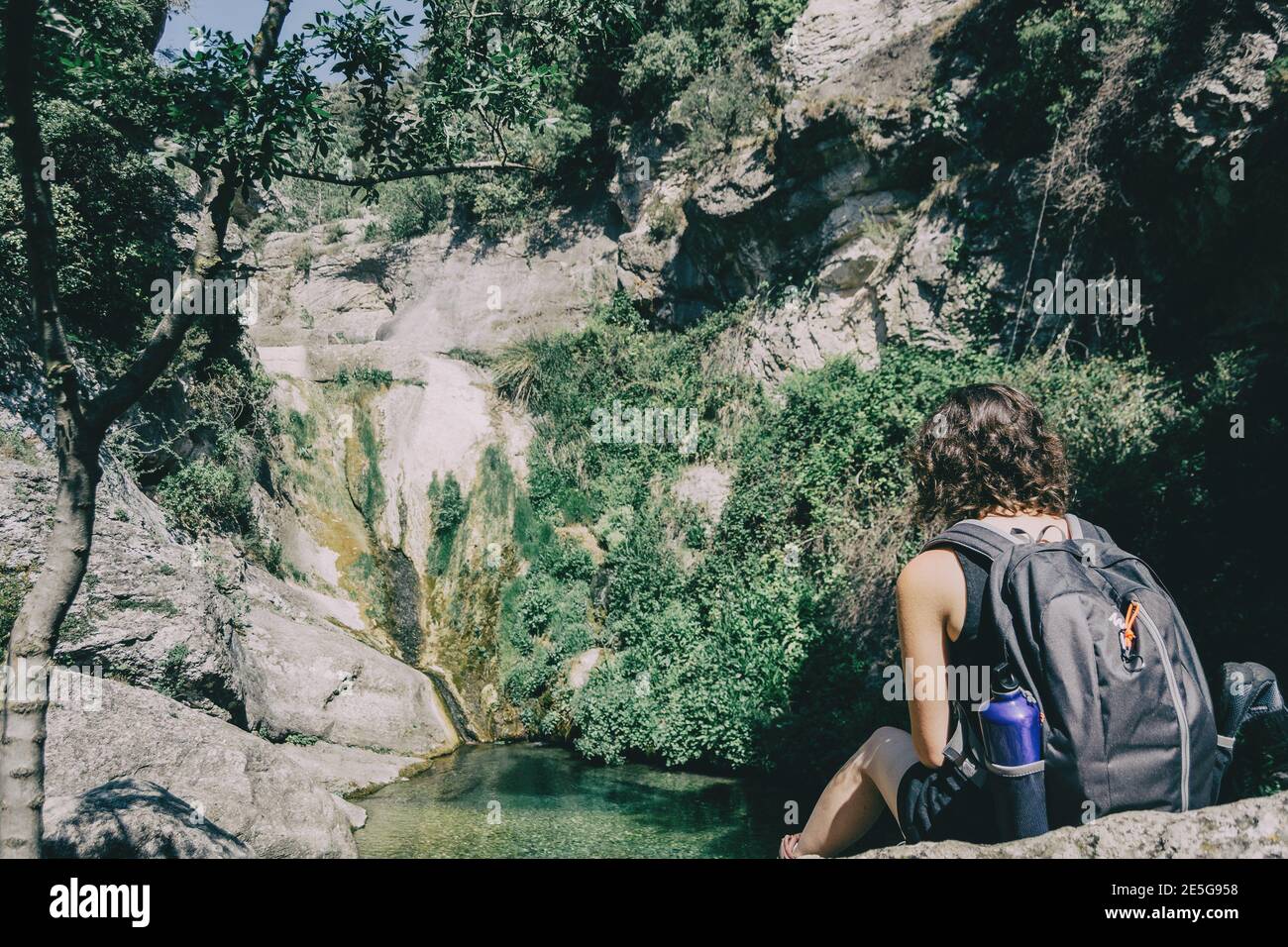 girl sitting on a rock looking at a landscape of a small waterfall on a ...