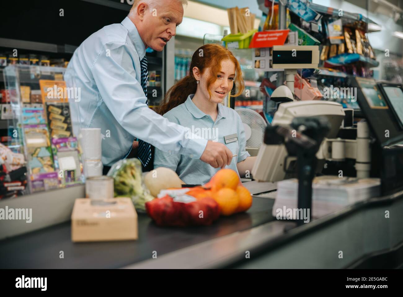 Supermarket manager training young worker at checkout counter. Senior ...