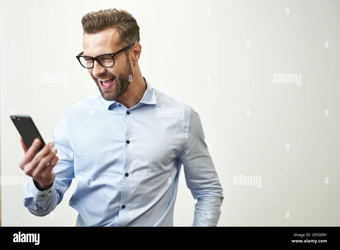 Happy young man looking at the screen of his phone and expressing ...