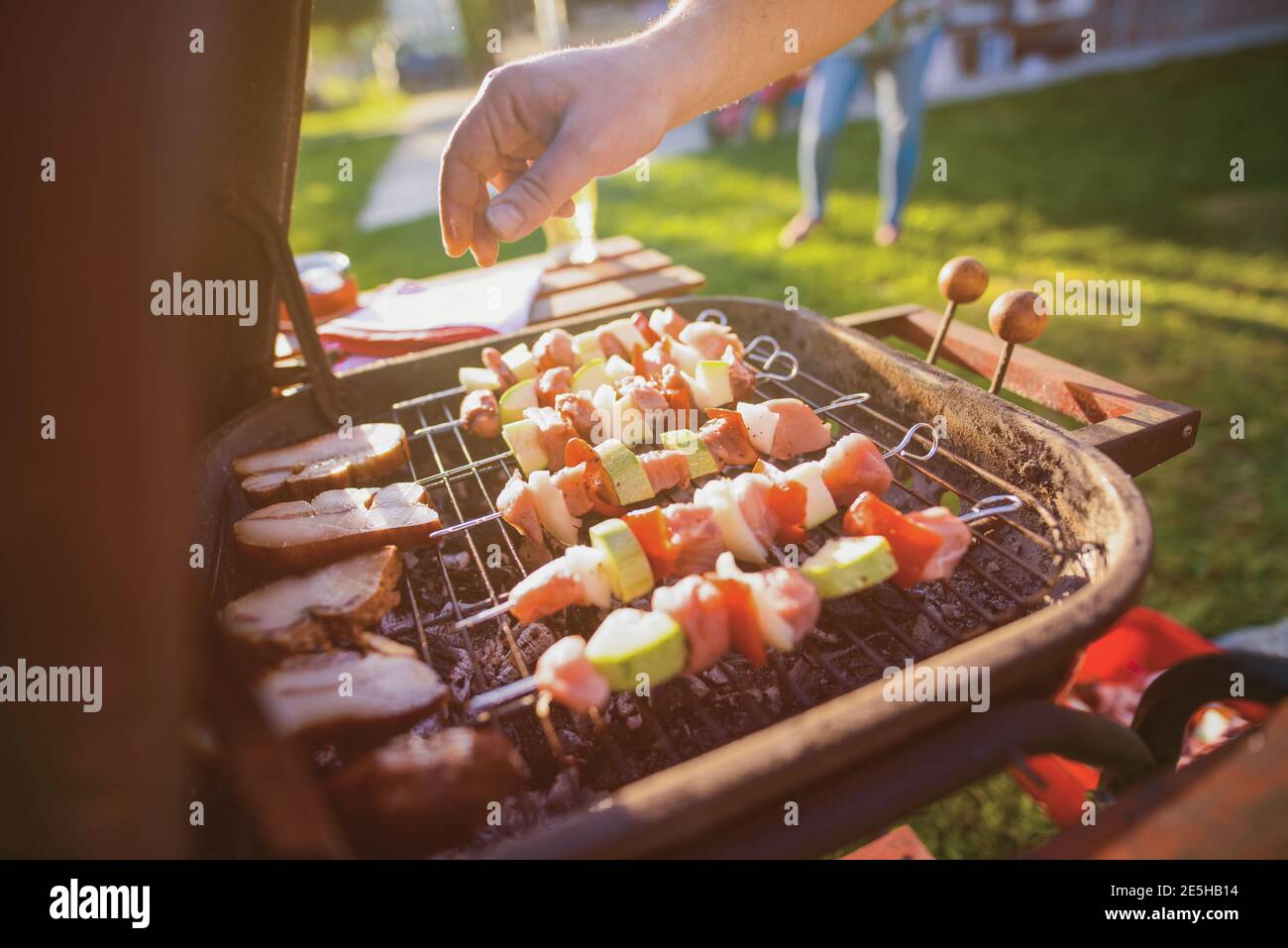 Close up of males hand turning meat and vegetable on barbeque grill ...