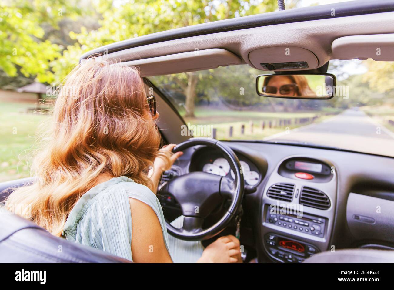 Pretty young woman driving convertible car on summer day. Wearing ...