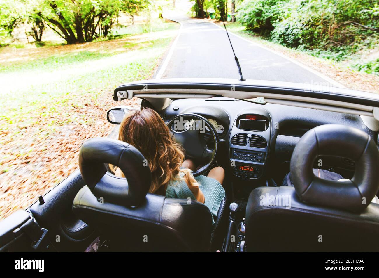 Young woman driving convertible car on summer day through nature ...