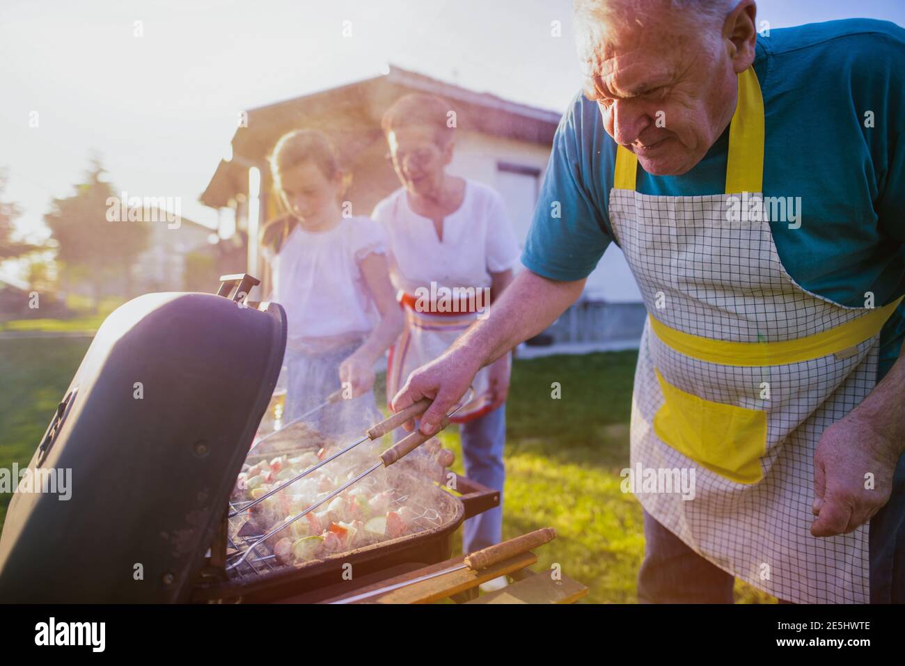 Older cheerful couple making barbeque in backyard. Spending some time ...