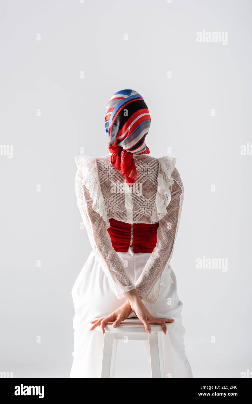 back view of stylish woman in headscarf sitting on stool isolated on ...