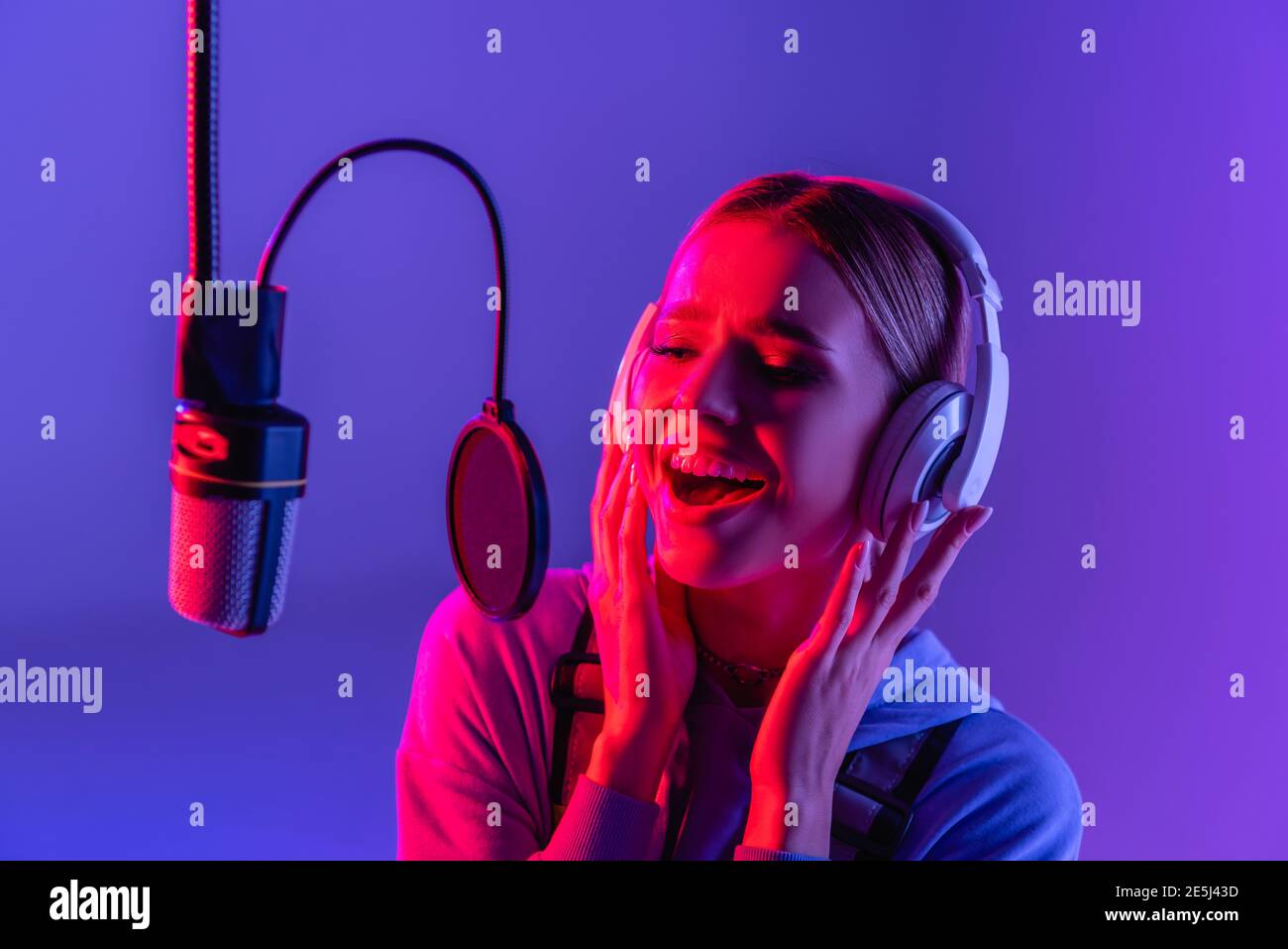young singer in wireless headphones recording song while singing in ...