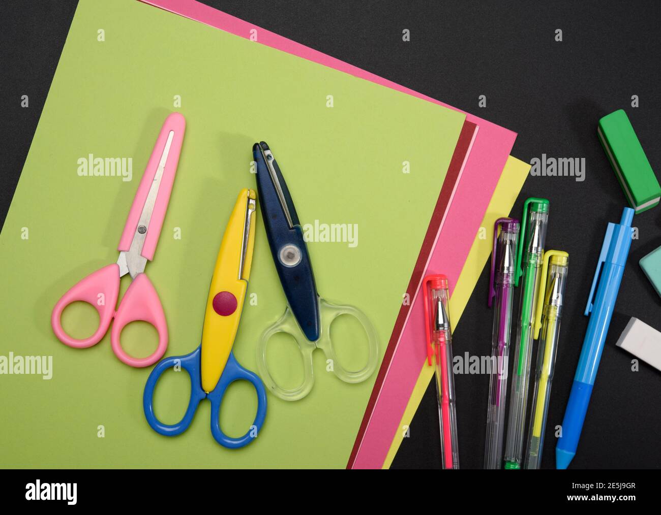 plastic scissors and colored paper on a black background, back to ...