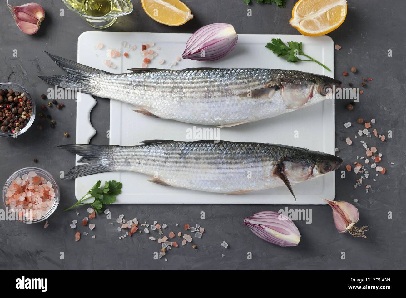 Two raw mullet with ingredients and seasonings on white plastic board ...