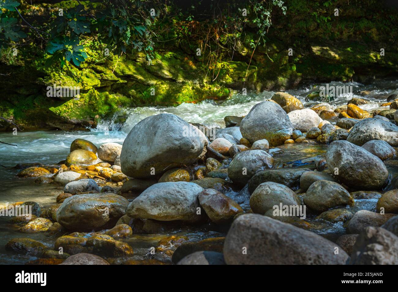 The mountain stream flows quickly between large stones and pebbles ...