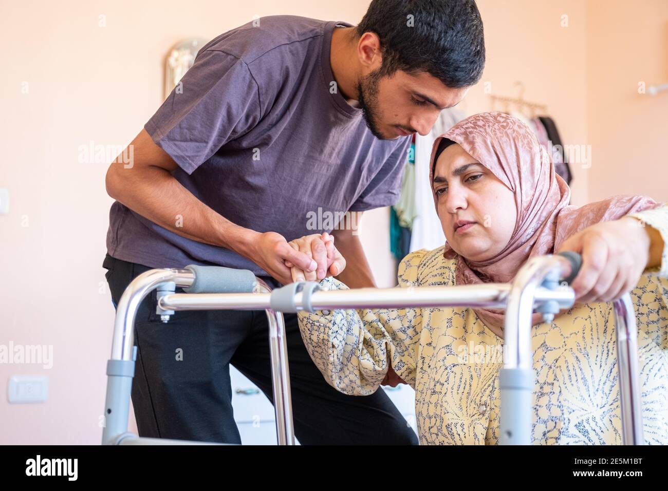 muslim woman with disability is trying to stand with her son's help ...