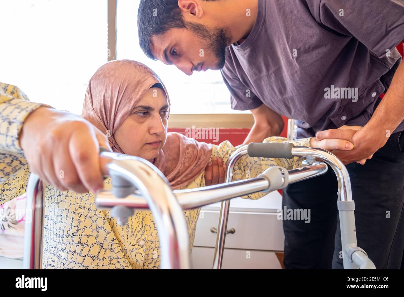 muslim woman with disability is trying to stand with her son's help ...