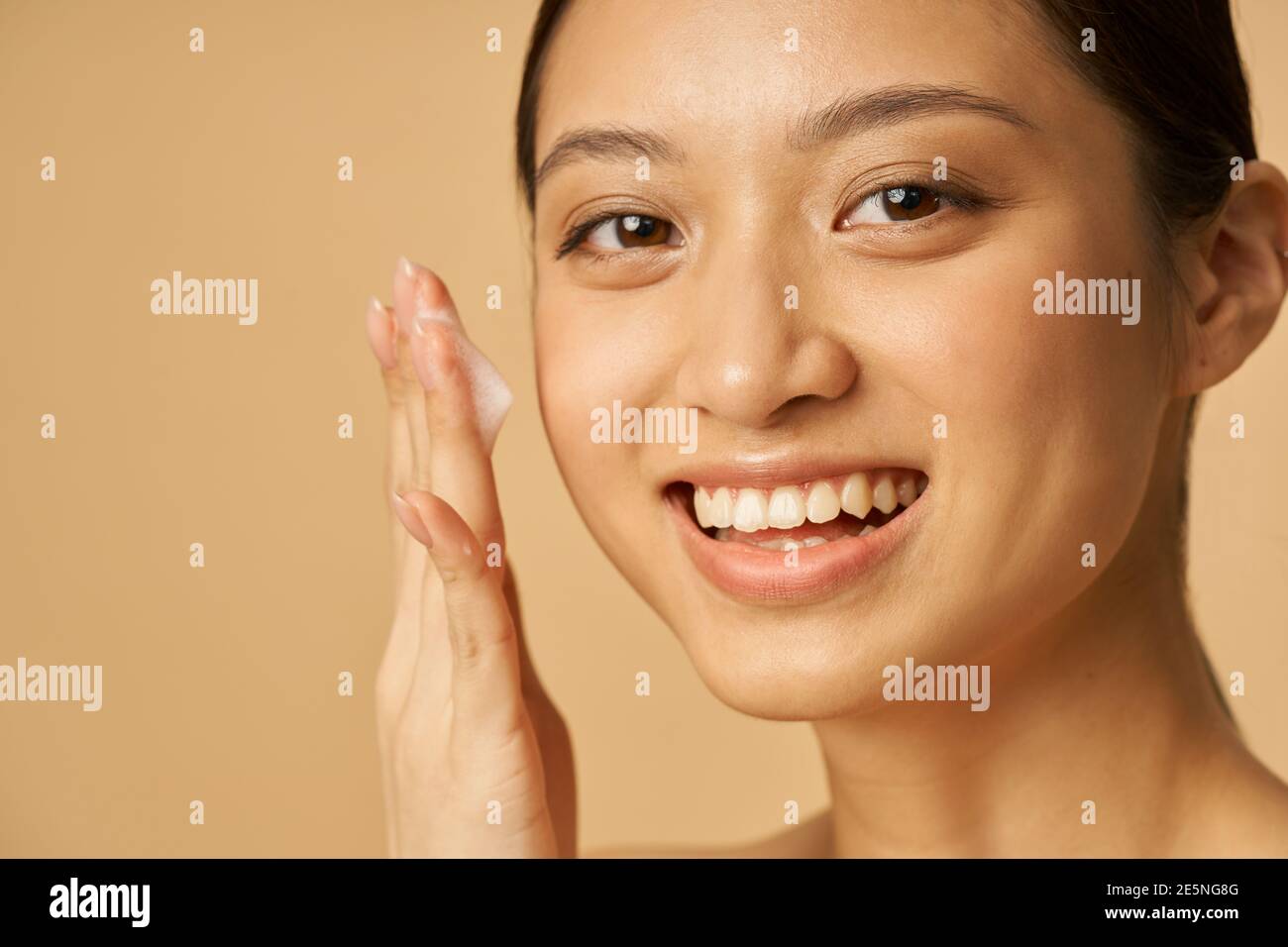 Studio portrait of lovely young woman smiling at camera while applying ...