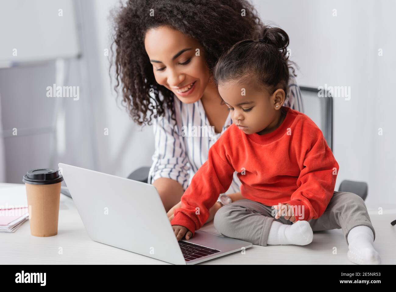 toddler african american child typing on laptop near cheerful mother ...