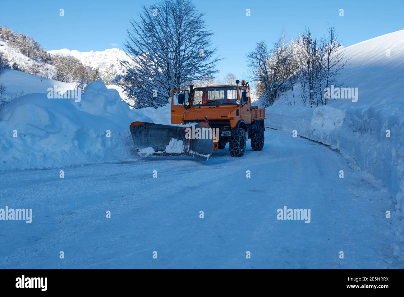 orange snow plow truck with snow chains stopped in a rural snowy road ...