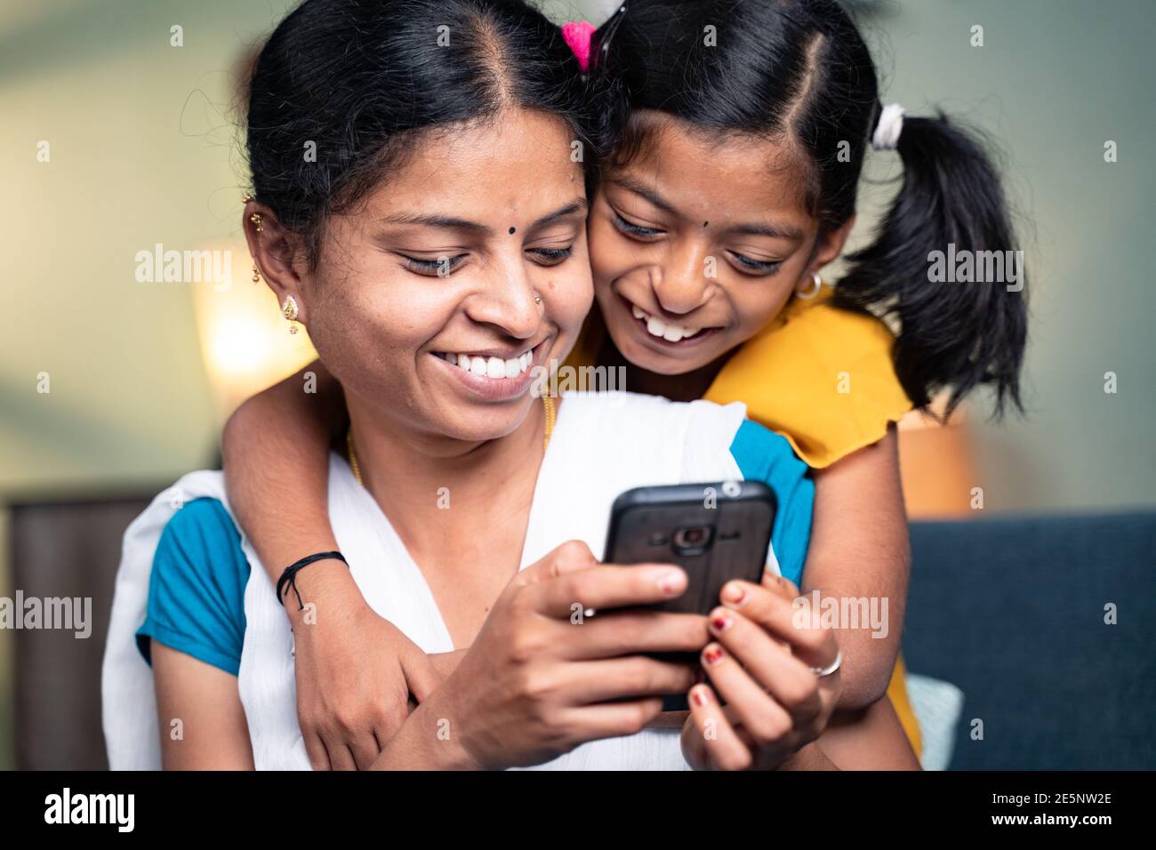 Young mother and her daughter busy in laughing by seeing something on mobile phone whlie ...