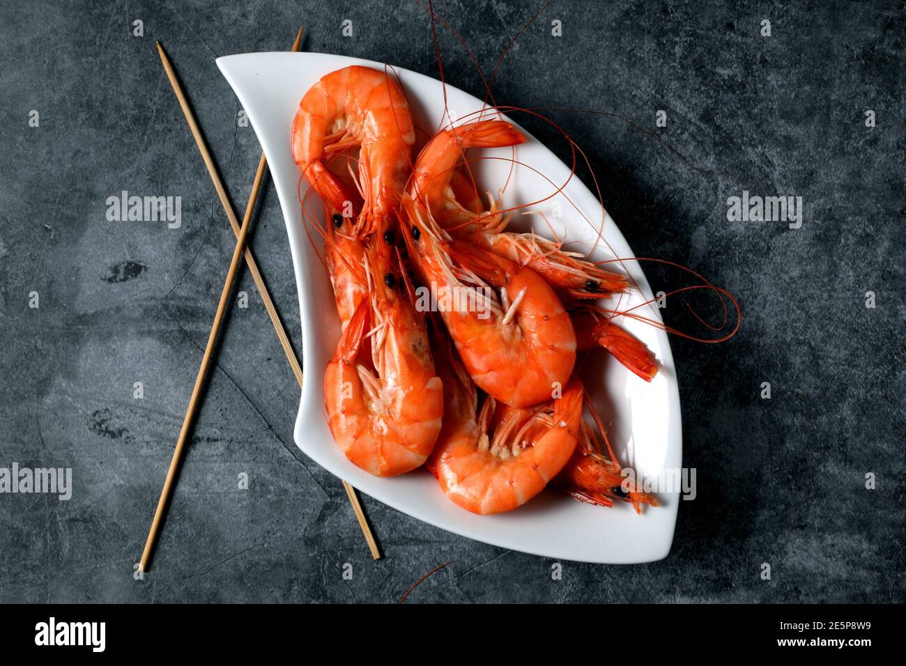Top view of cooked shrimp on a white platter with sticks on a gray ...