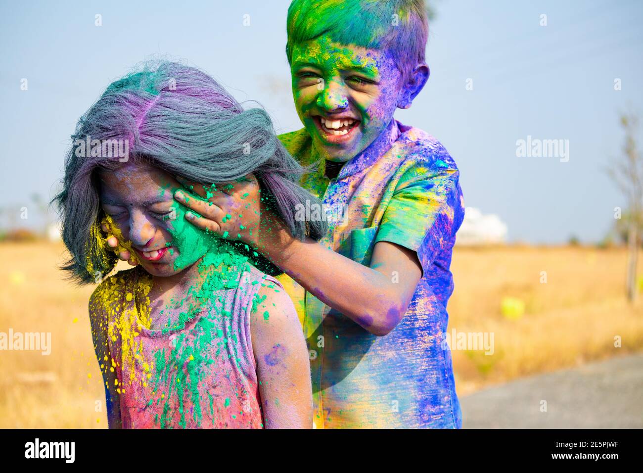 Young kid from the back applying holi colors to girls face during holi ...