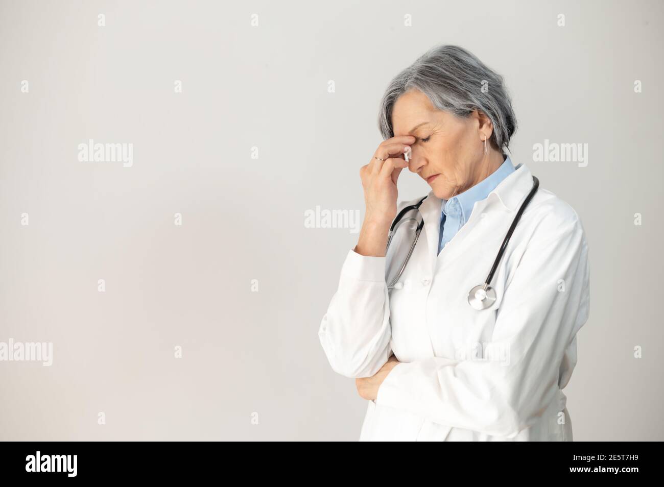Stressed senior female doctor with a stethoscope in a medical robe ...