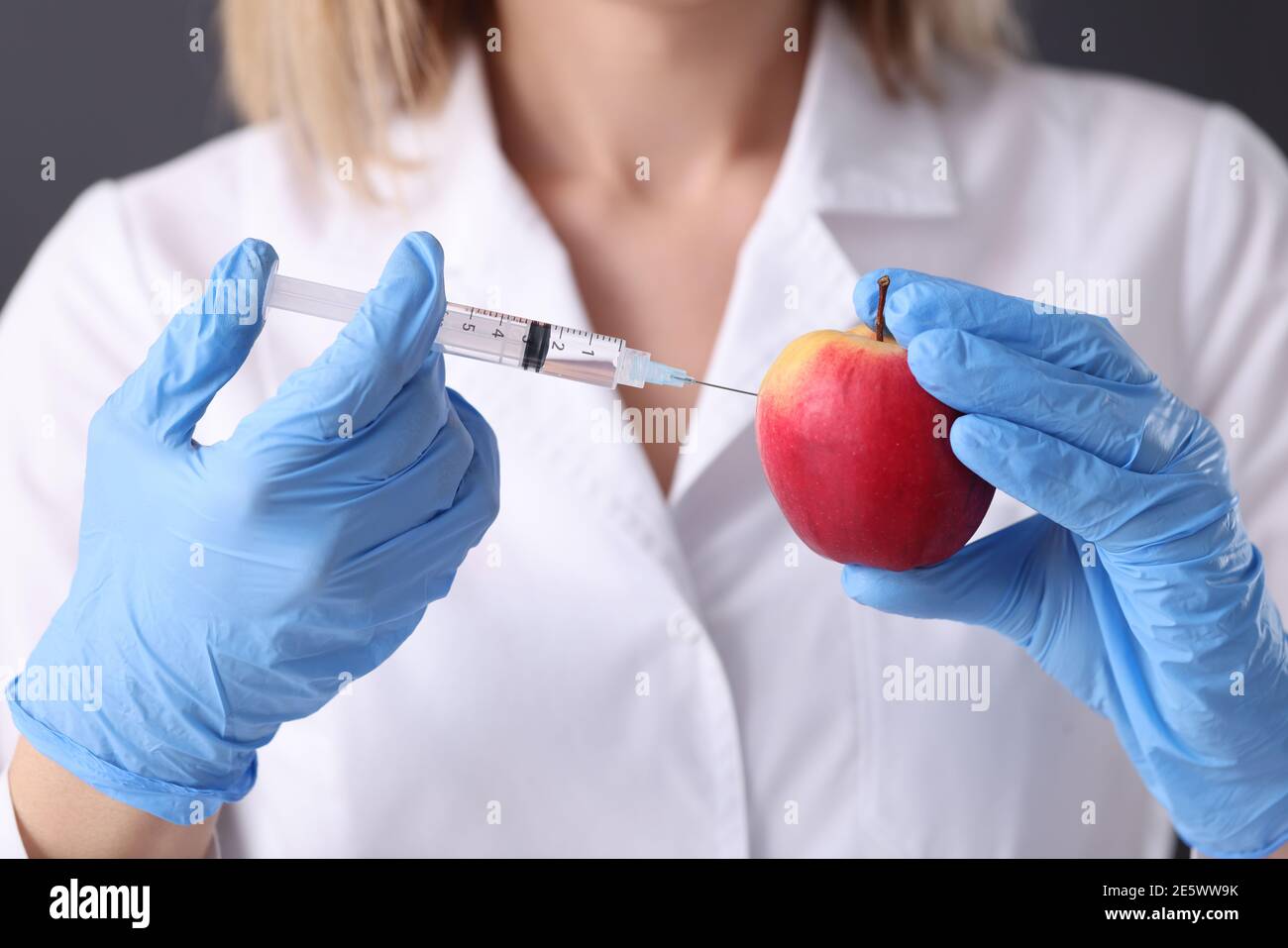 Woman scientist in rubber gloves making injection into apple closeup ...