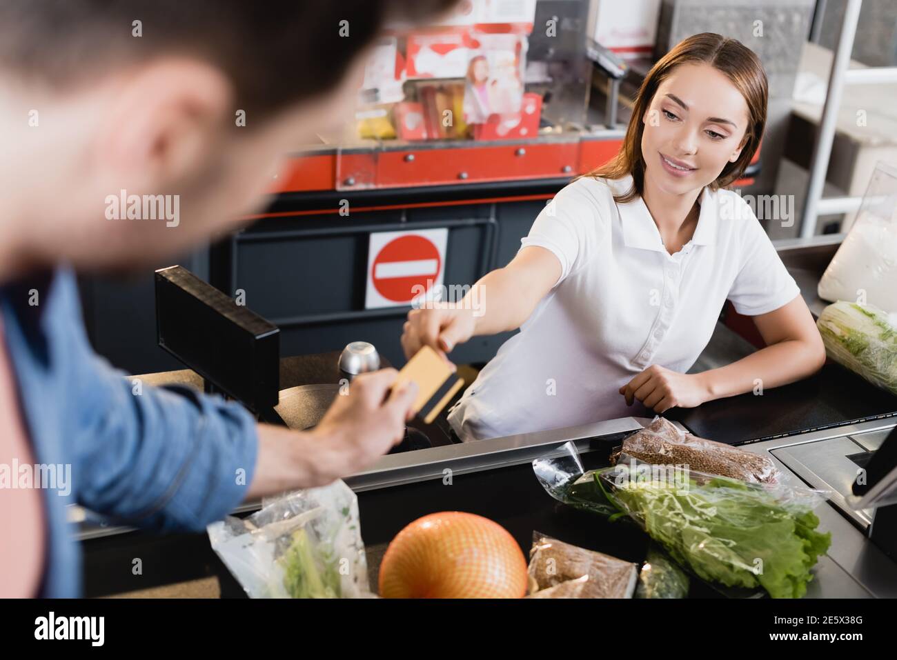 Smiling cashier taking credit card from customer rear groceries on ...
