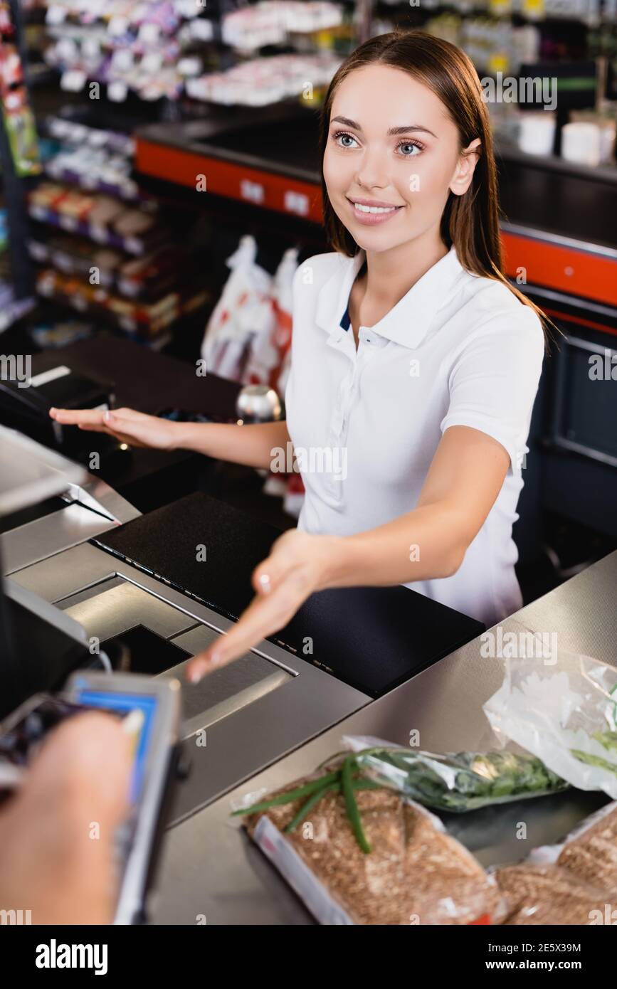 Smiling cashier pointing with hand while customer paying with ...