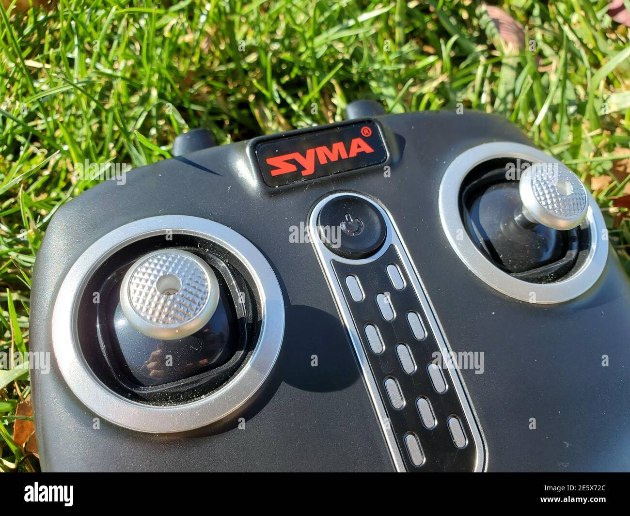 Close-up of a drone controller on a grass lawn displaying the Syma logo ...