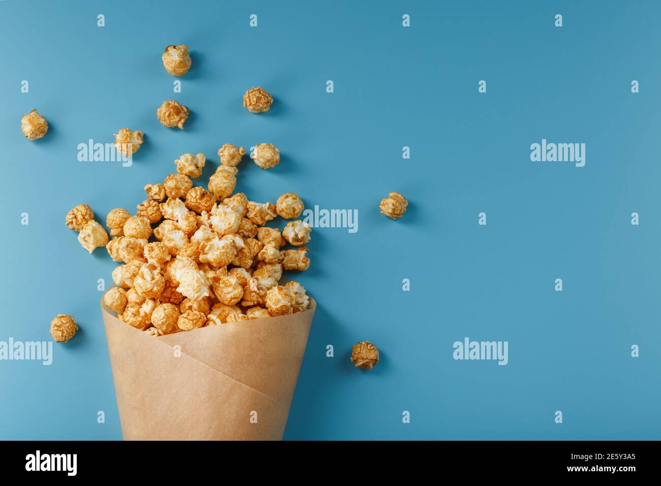 Popcorn in caramel glaze in a paper envelope on a blue background ...