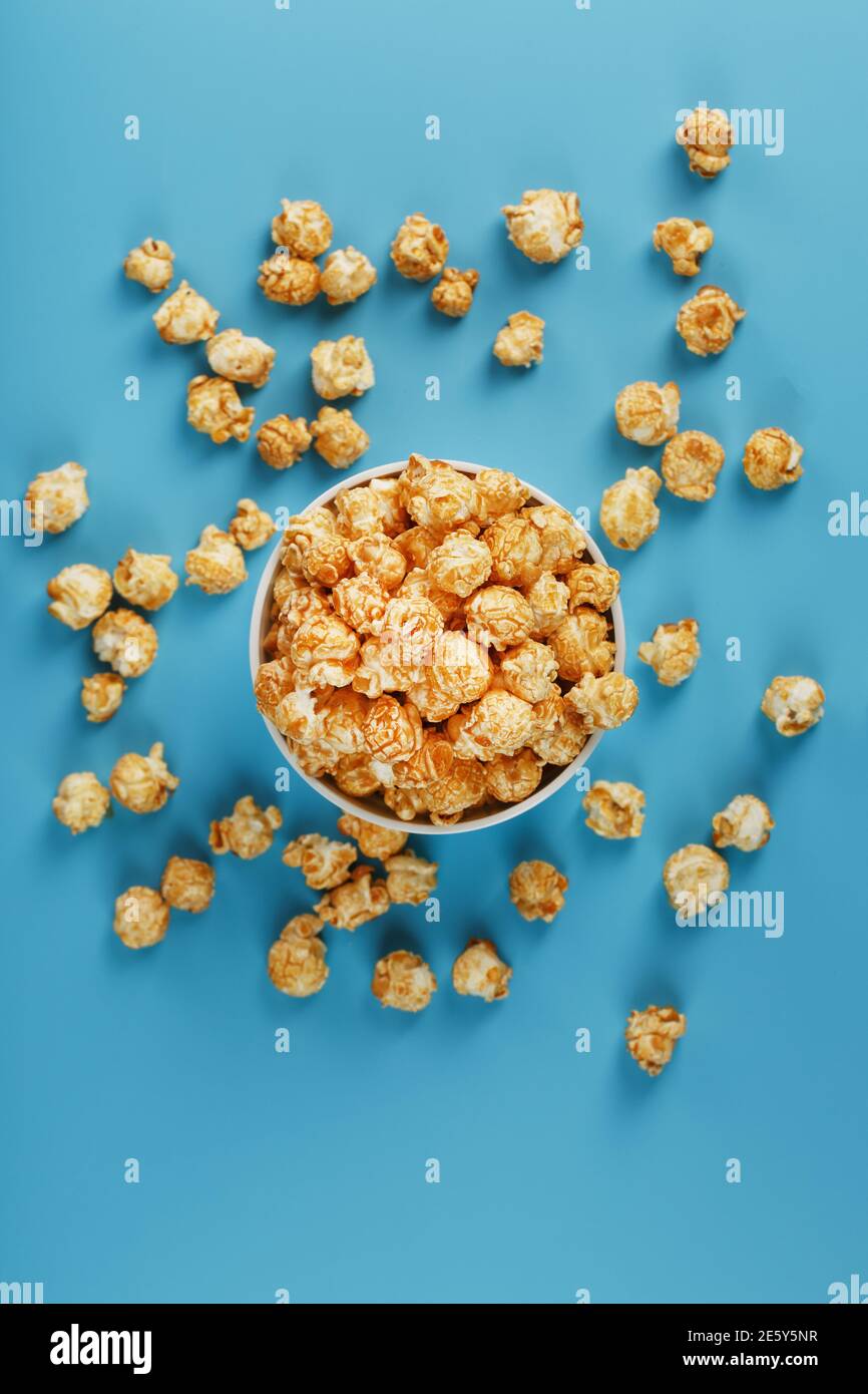 Caramel popcorn in a white glass cup with scissors on a blue background ...
