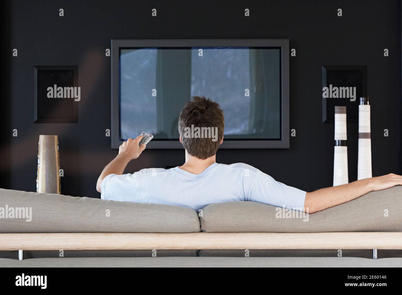 Rear view of young man using remote control while sitting on couch in ...