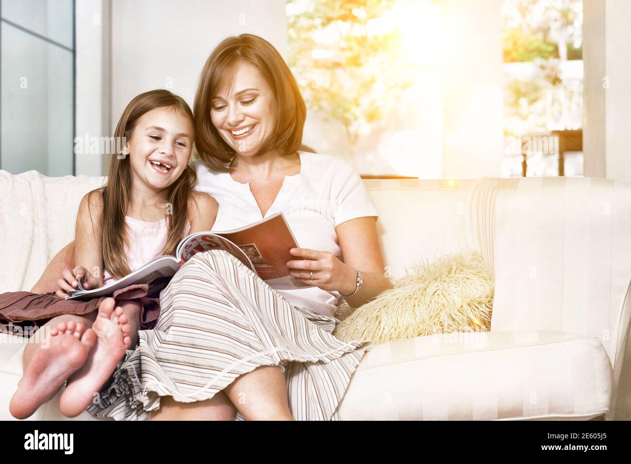 Cheerful mother and daughter reading book in living room during lockdown Stock Photo - Alamy