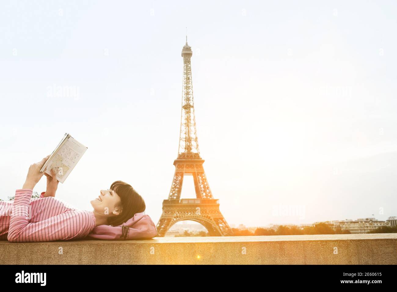 Young woman lying on balcony and reading book in front of Eiffel Tower ...