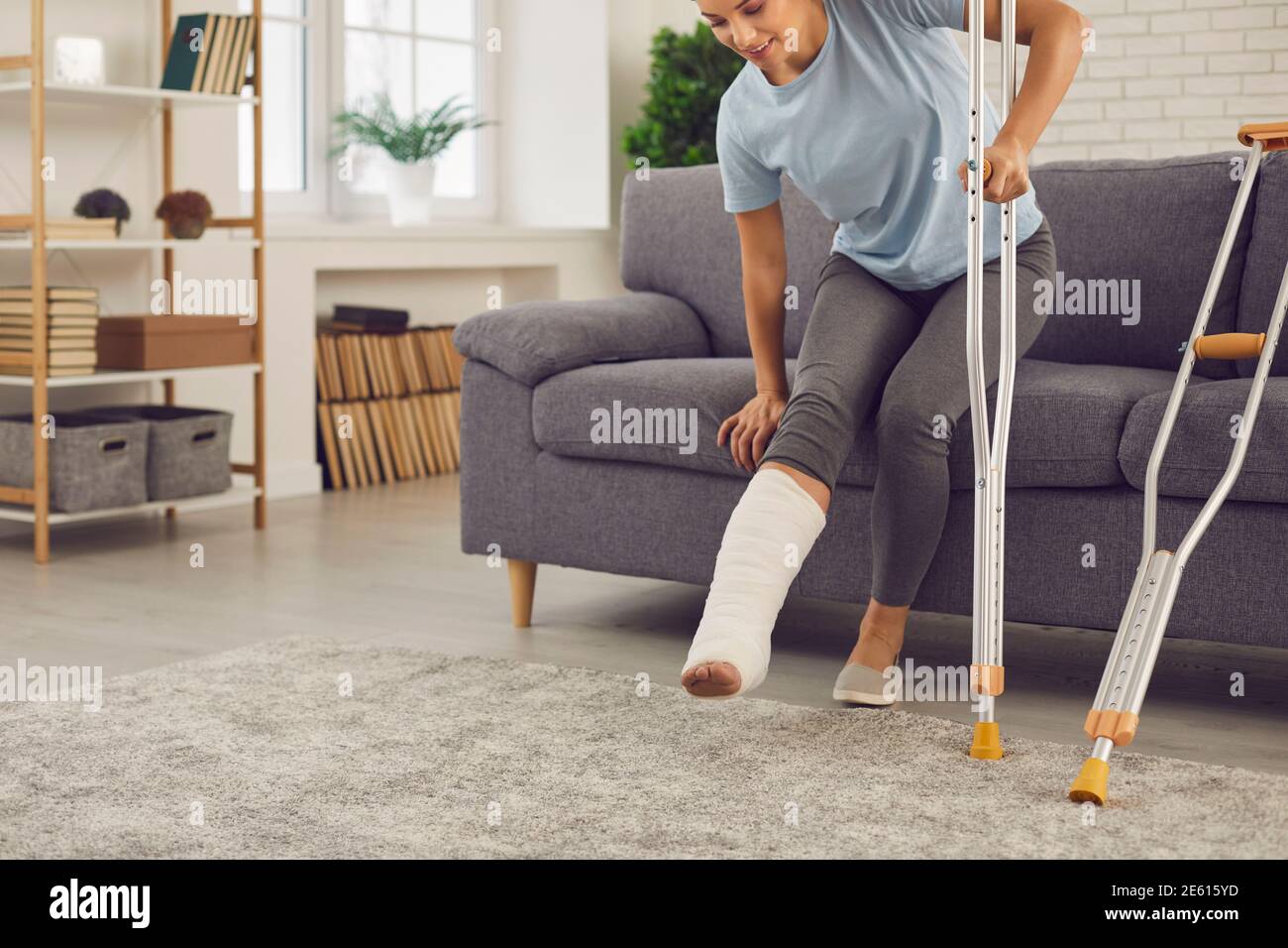 Young woman with broken leg in cast tries to stand up and walk with ...