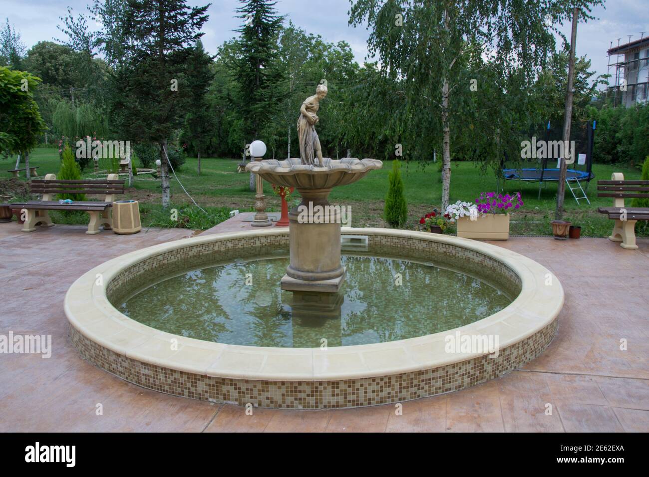 Beautiful round water fountain in a garden with plants, flowers and ...