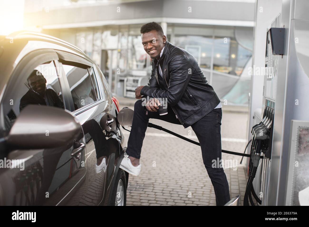 Happy handsome young African American man on a gas station, leaning on ...