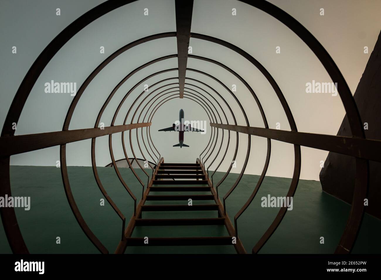 A circular steel ladder with a plane in the sky at sunset Stock Photo ...