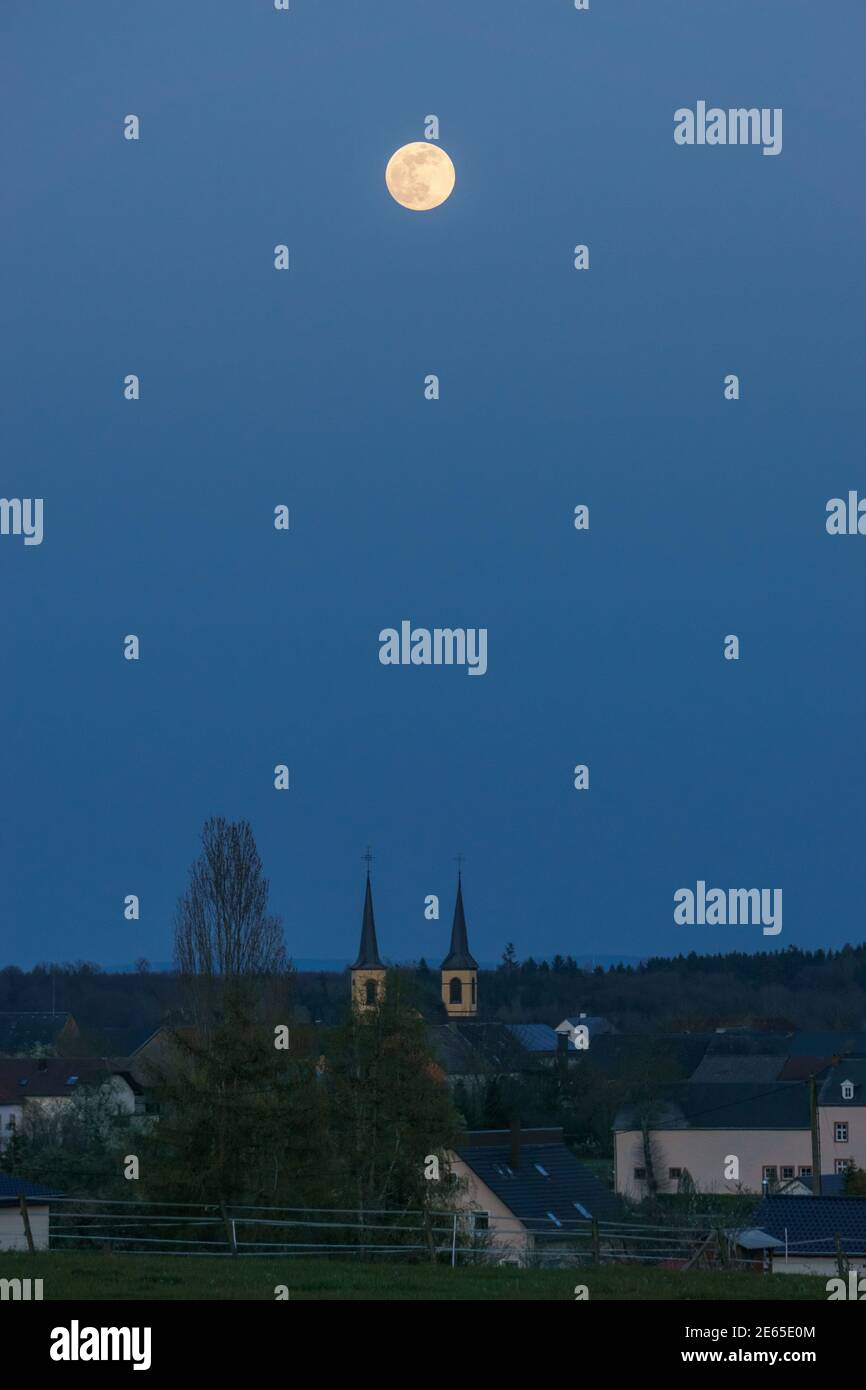 full moon rising at blue hour over rural countryside outside village ...