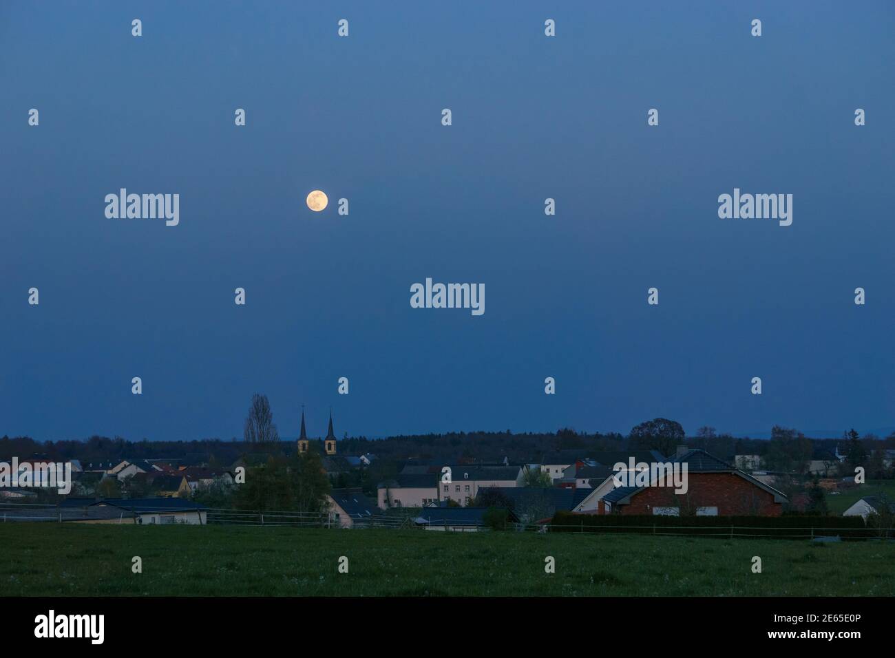 full moon rising at blue hour over rural countryside outside village ...