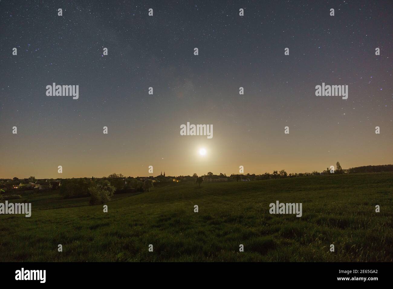 moon and milkyway over meadow with trees outside a german village in ...