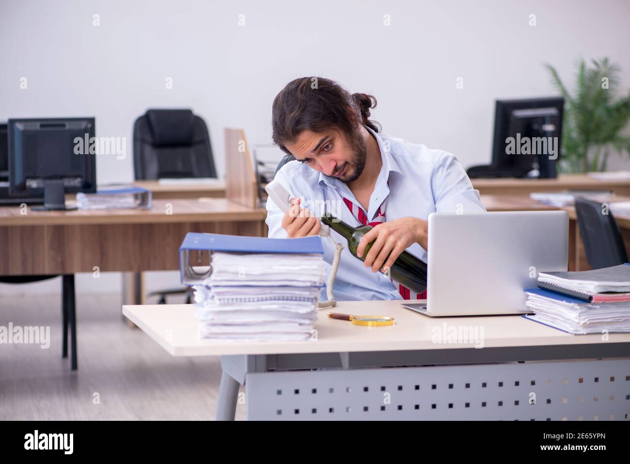 Young male employee drinking alcohol at workplace Stock Photo - Alamy