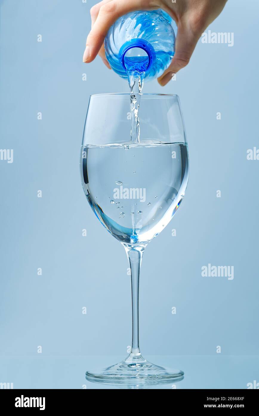 Pouring clean drinking water from blue plastic bottle into glass on ...