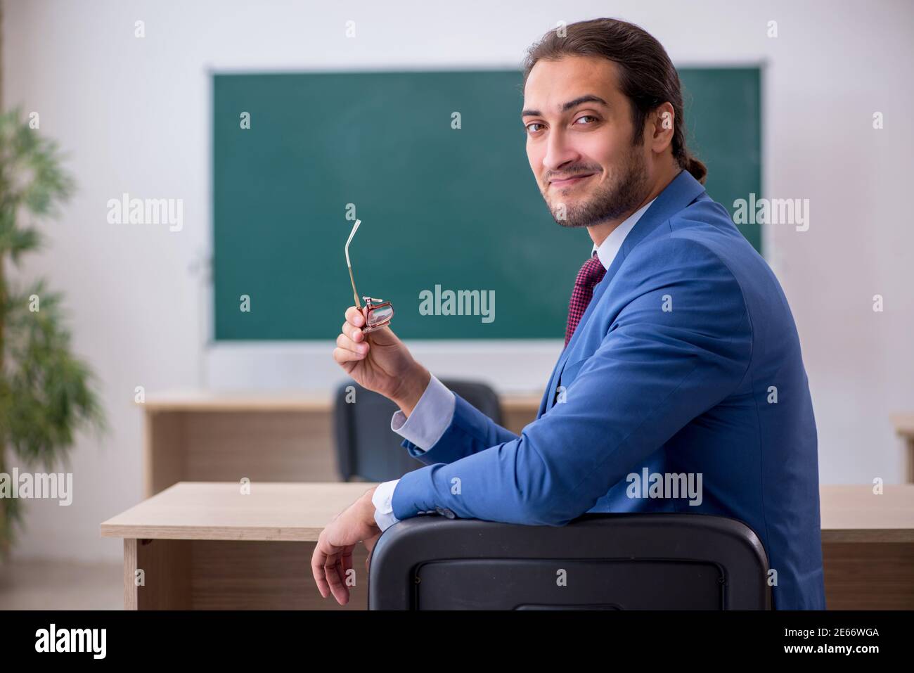 Young teacher in suit in front of green board Stock Photo - Alamy