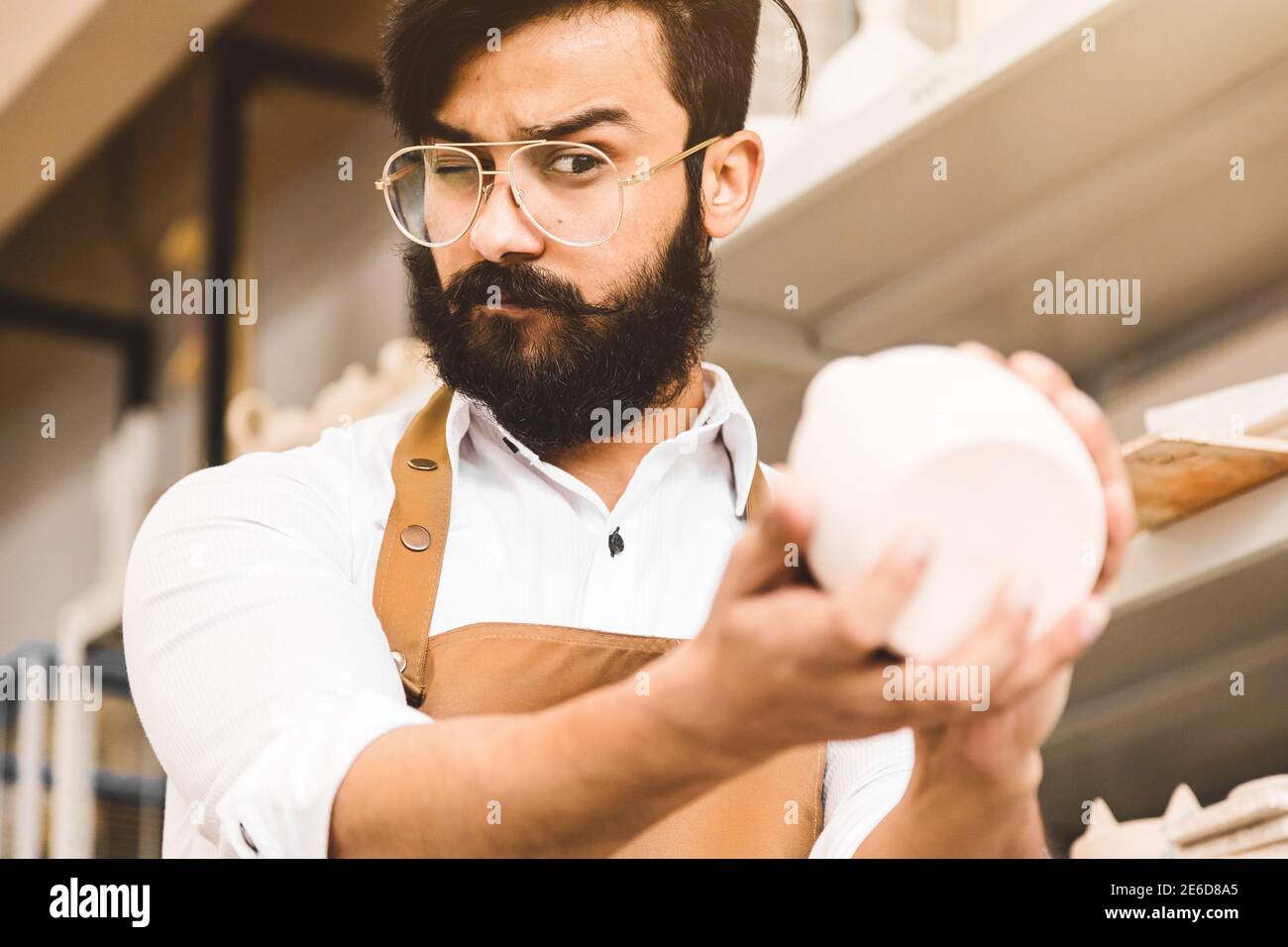 A young attractive male potter with a beard and mustache works in his ...