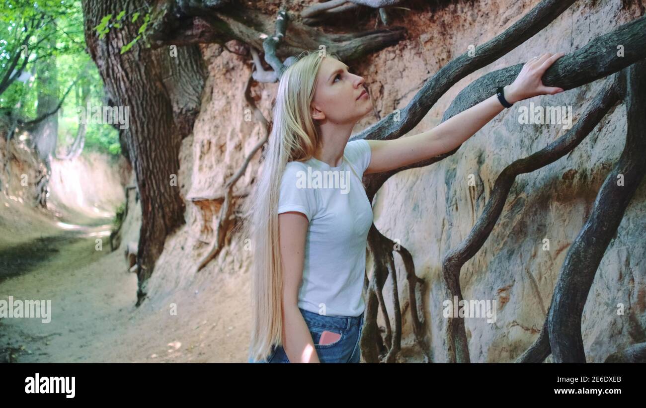 Young blonde woman looking on exposed tree roots in natural loess ...
