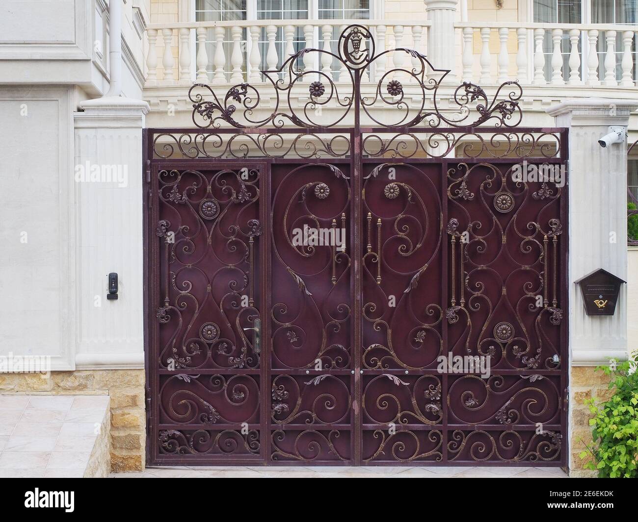 An iron burgundy fence with forged gilded pattern is located in front ...