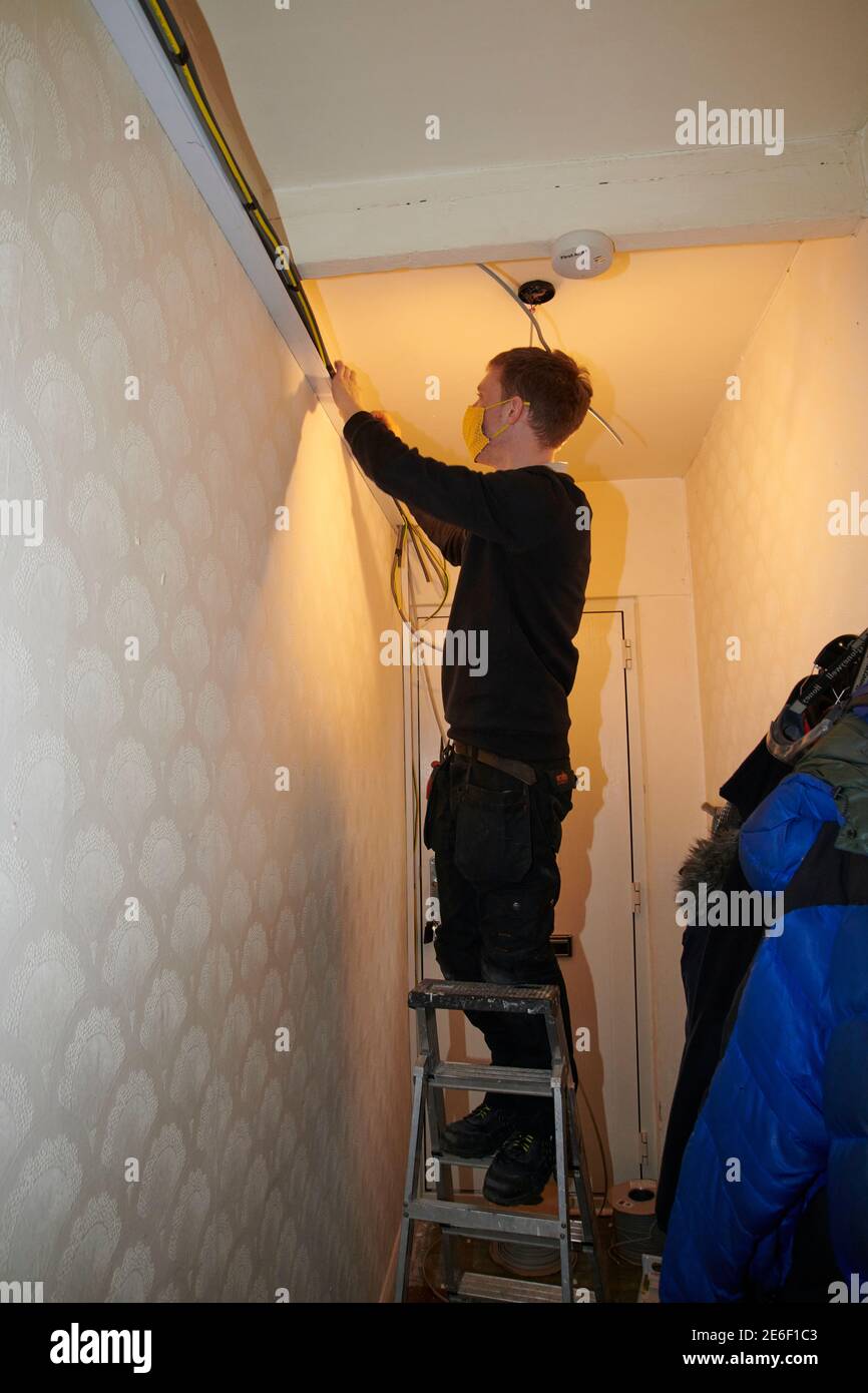 Electrician fitting a new mains electricity cable to a house with face ...