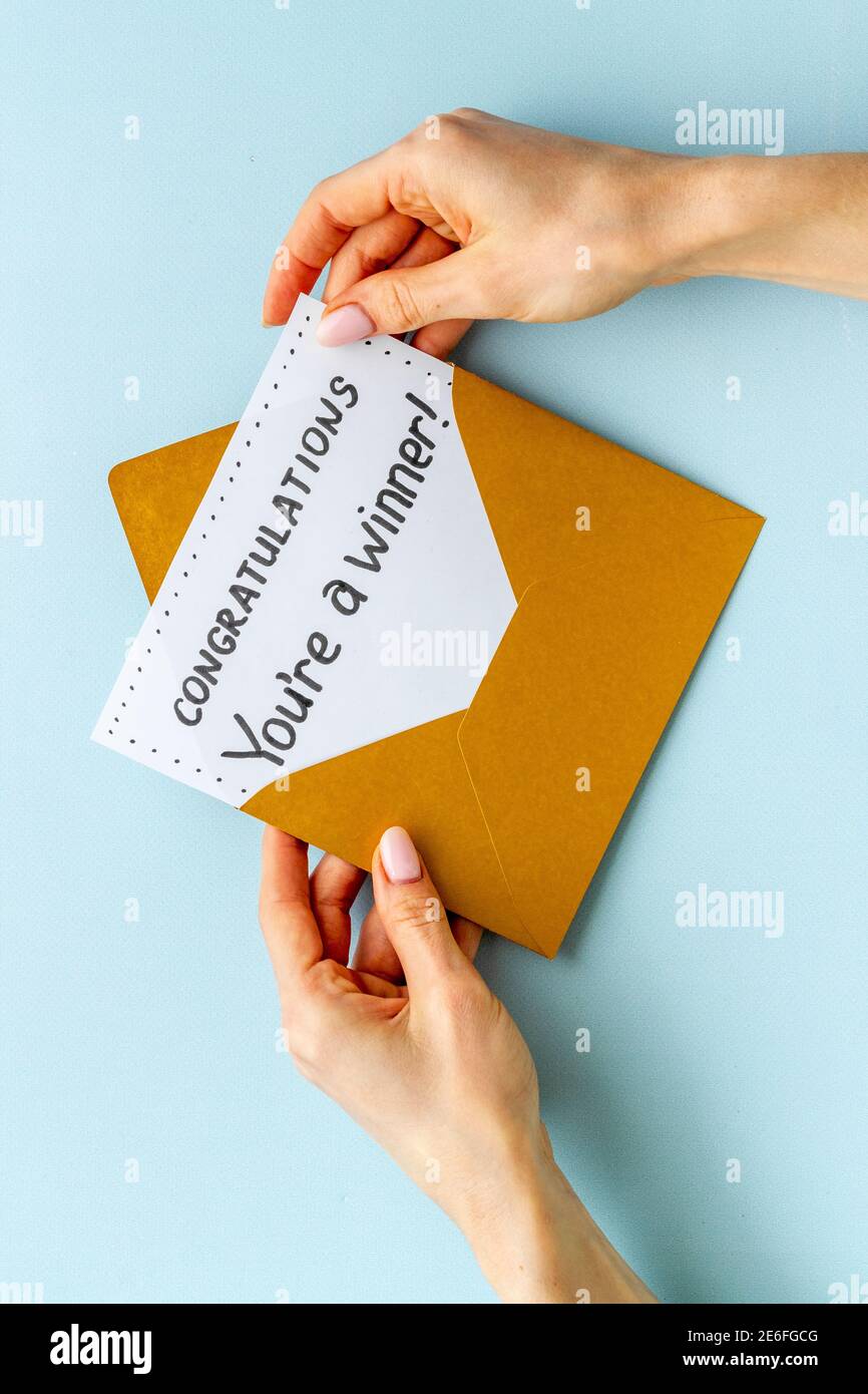 Hands holding award congratulation card in golden envelope. Text You're ...